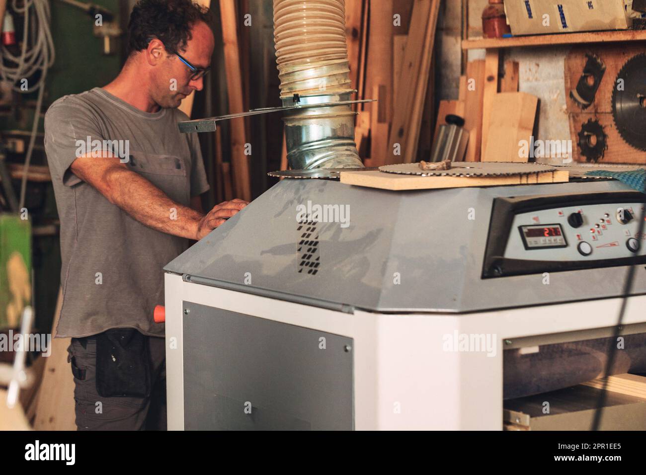 Carpenter in a messy corner of the woodshop, with lots of lumber ...