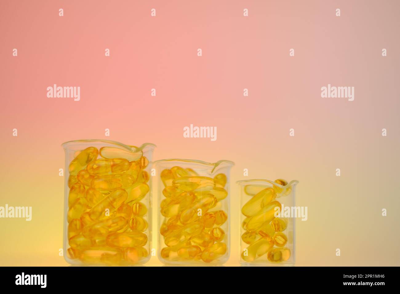 Yellow omega oil capsules in transparent containers on a pink ...