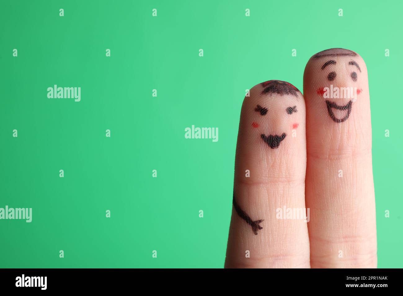 Two fingers with drawings of happy faces on green background, space for ...