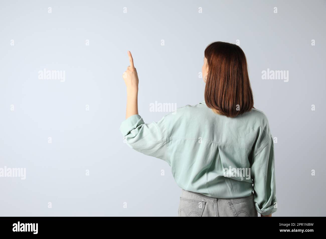 Young girl pointing on white background, back view. Space for text ...