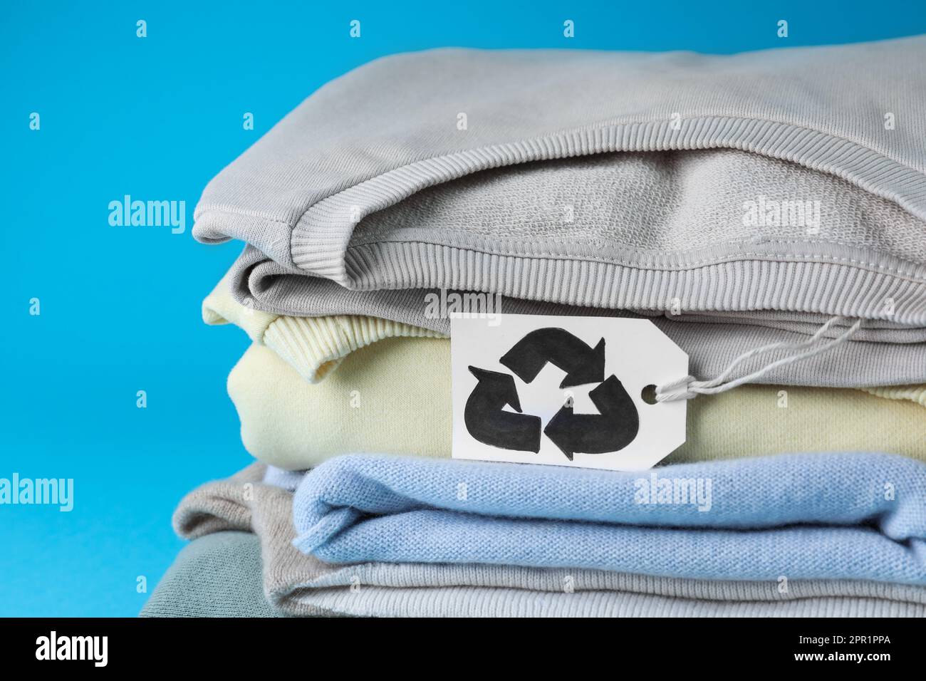 Stack of clothes with recycling label on light blue background, closeup ...