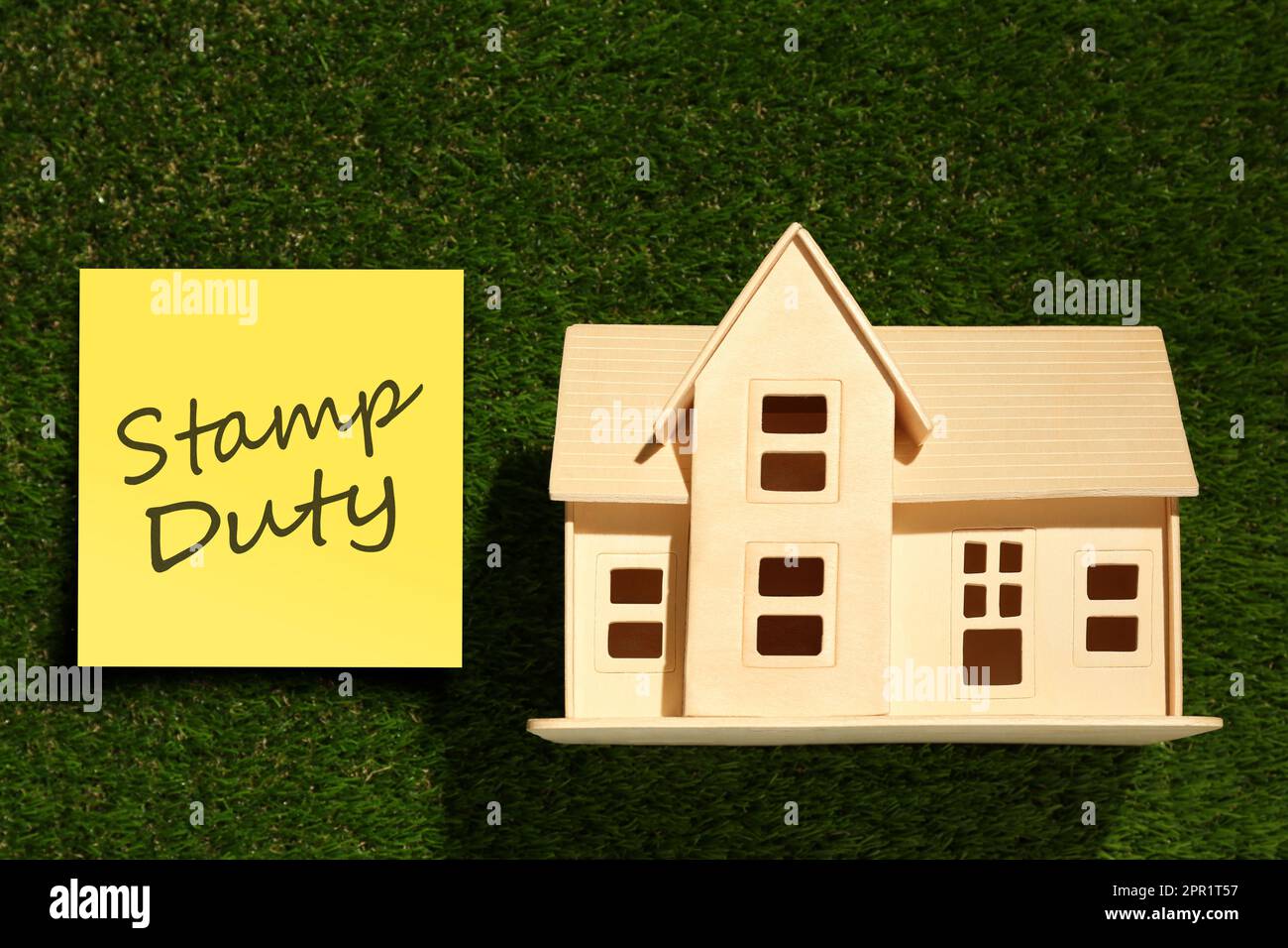 Wooden house model ans sticky note with text Stamp Duty on green grass ...