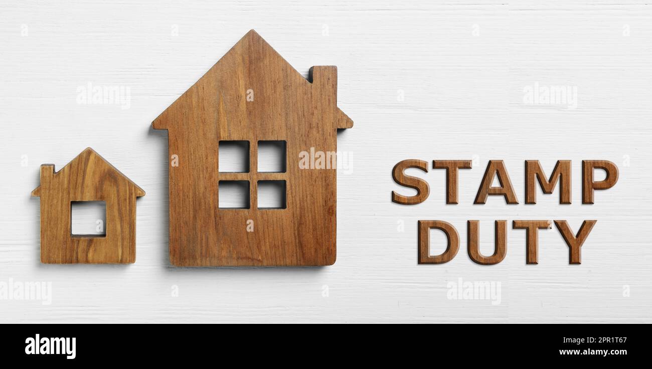 Stamp duty. Small and big house figures on white wooden background ...