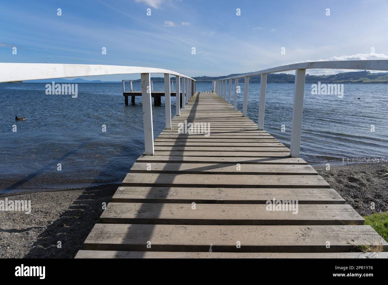 leading lines of railing and shadow on old wooden jetty projecting into ...