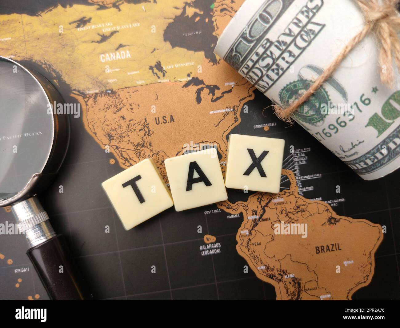 Magnifying glass and banknotes with the word TAX on a world map ...