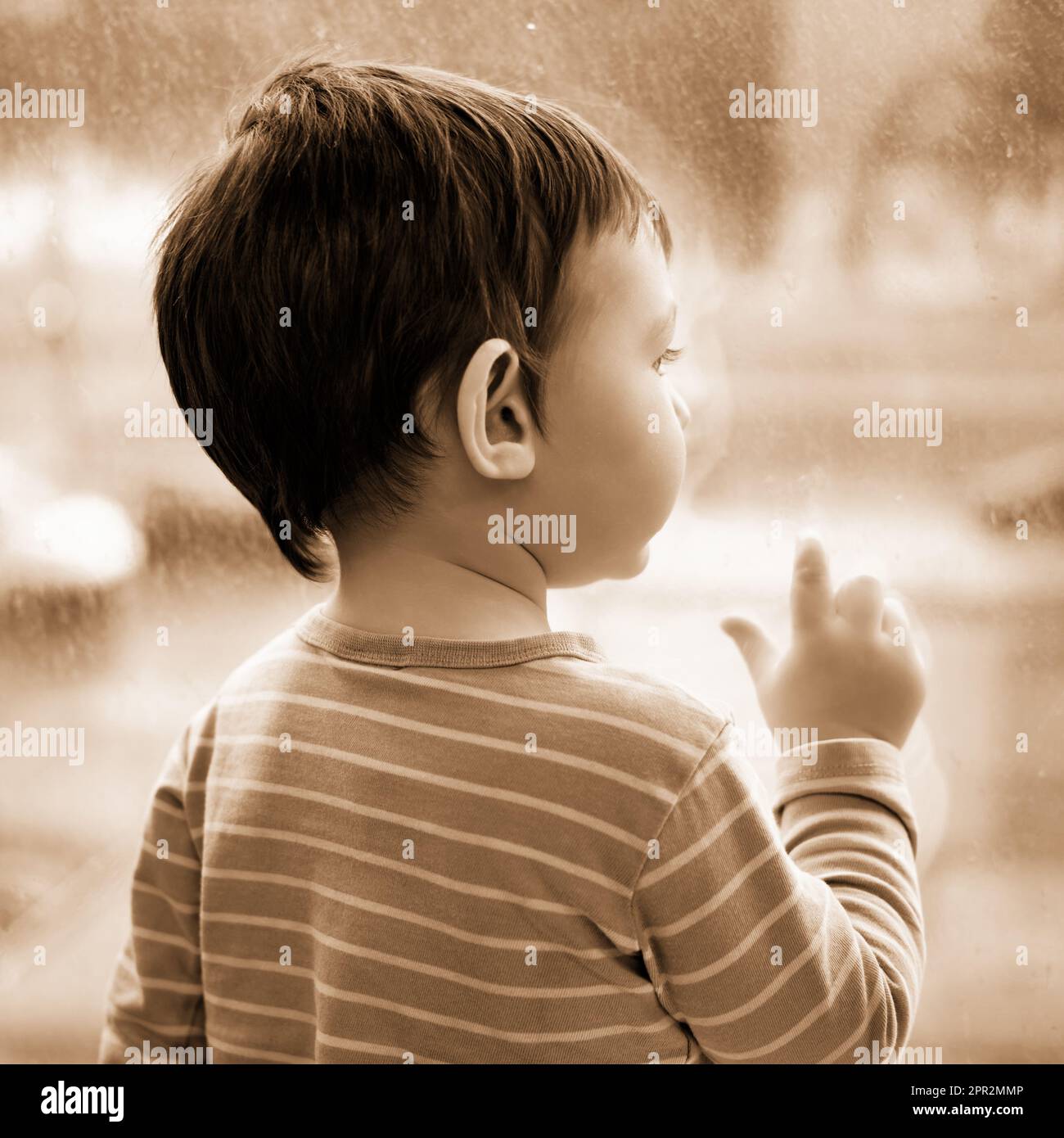 Toddler baby stands at the window and looks at the road. A happy child ...