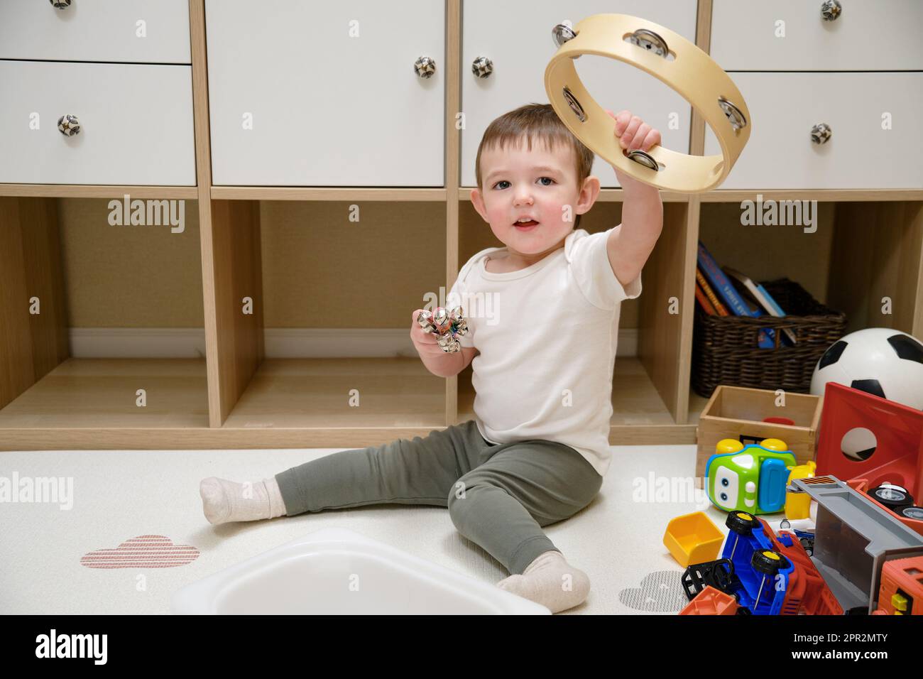 Toddler baby plays the tambourine while sitting on the floor in the ...