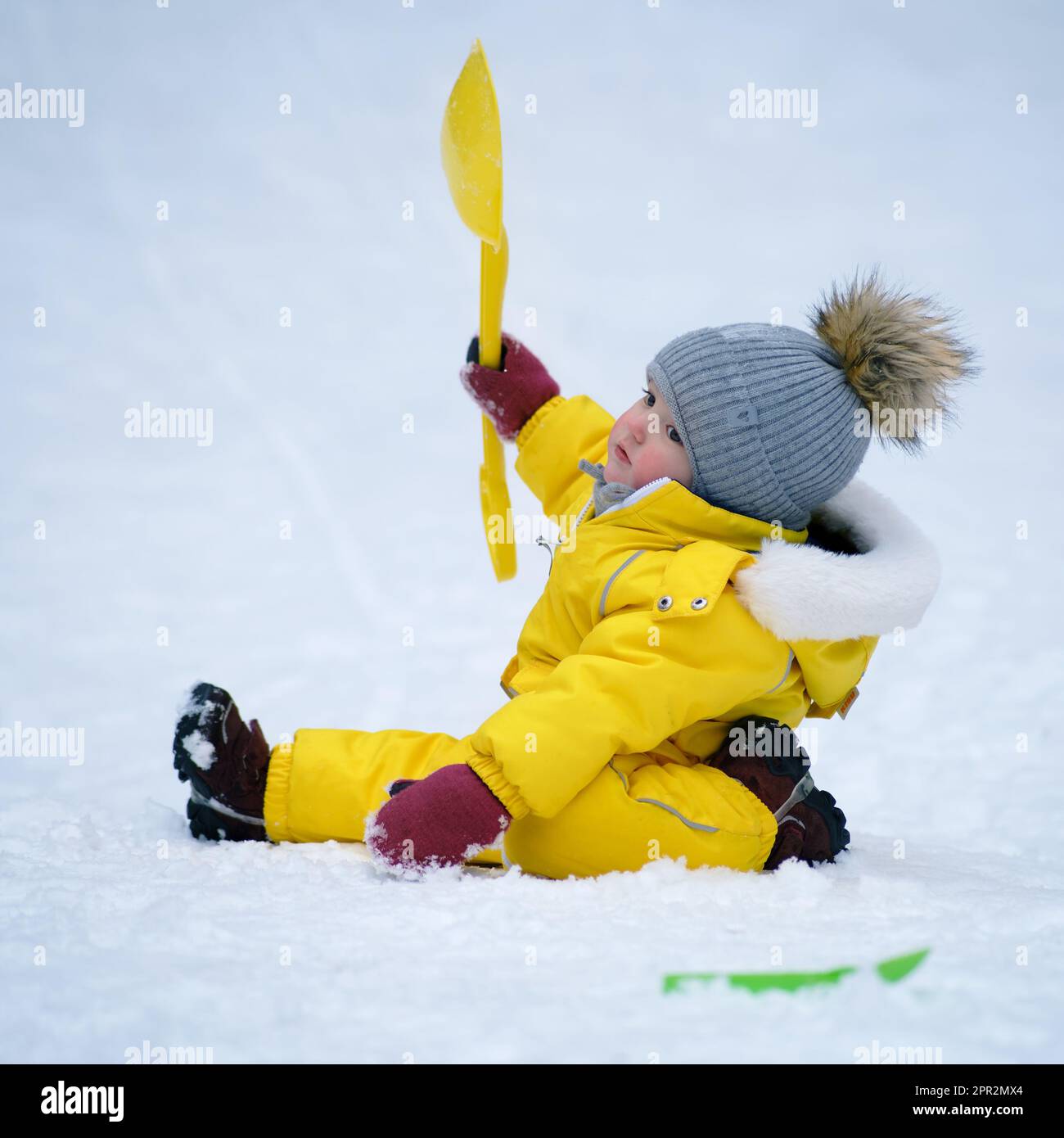 Happy toddler baby is playing with a toy in the snow in a yellow ...
