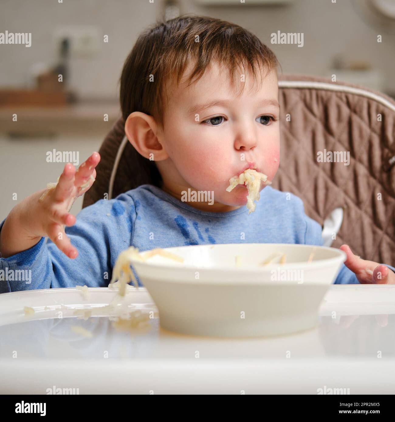A funny child is eating a grated apple with his mouth full while ...