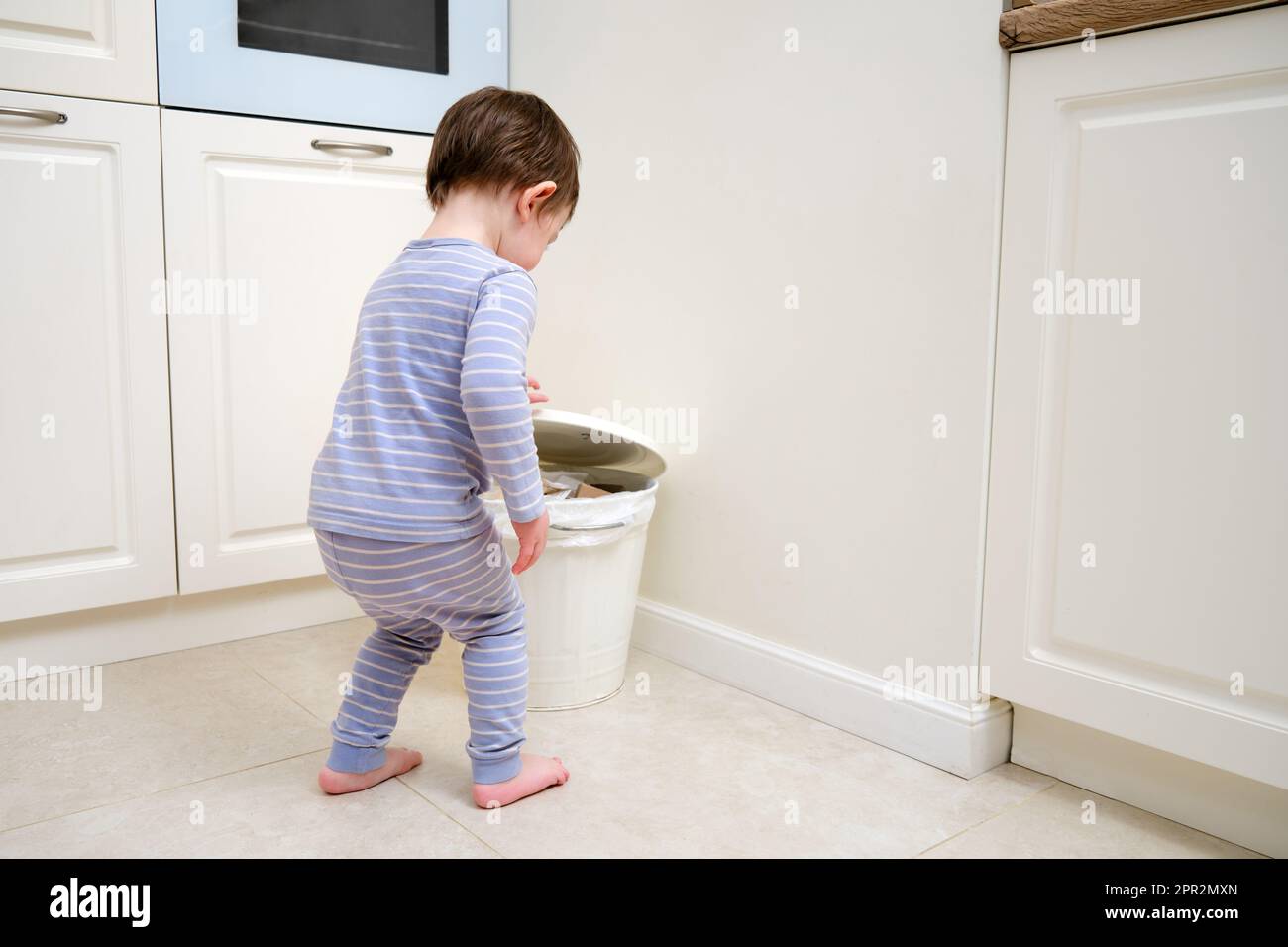 Toddler baby throws garbage in the trash can. A happy child lifts the ...