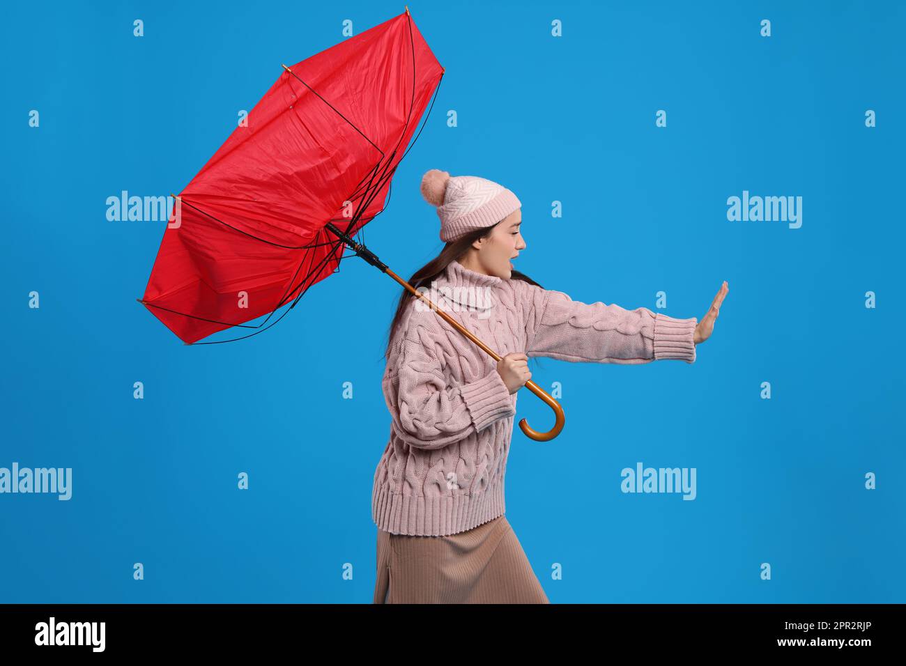 Young woman with umbrella caught in gust of wind on light blue ...