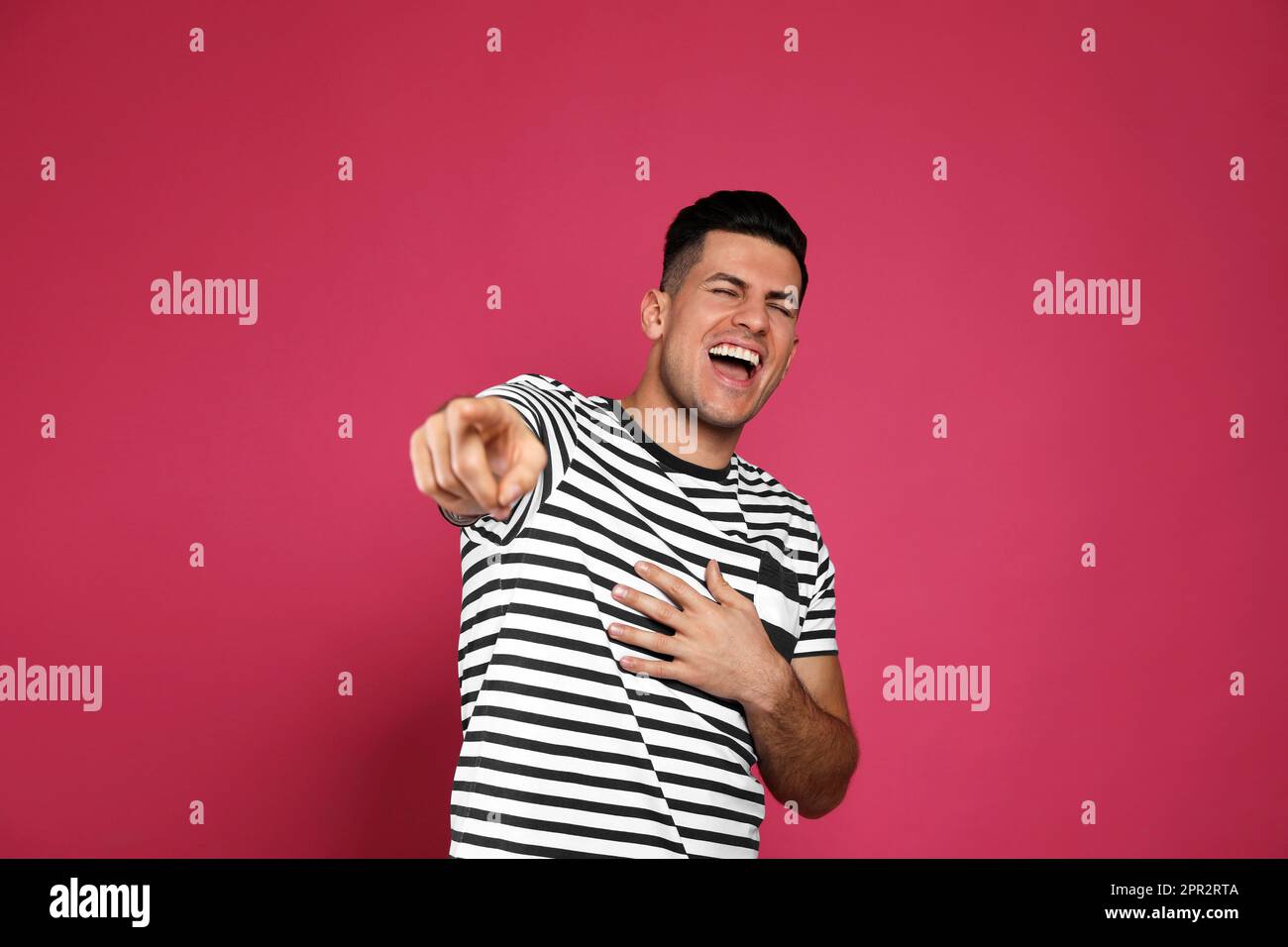 Handsome man laughing on maroon background. Funny joke Stock Photo - Alamy