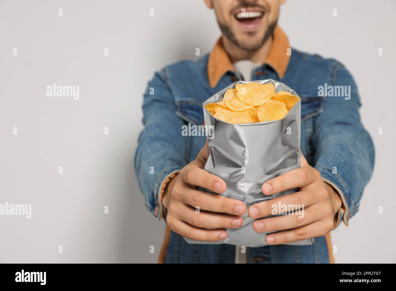 Handsome man with potato chips against light grey background, closeup ...