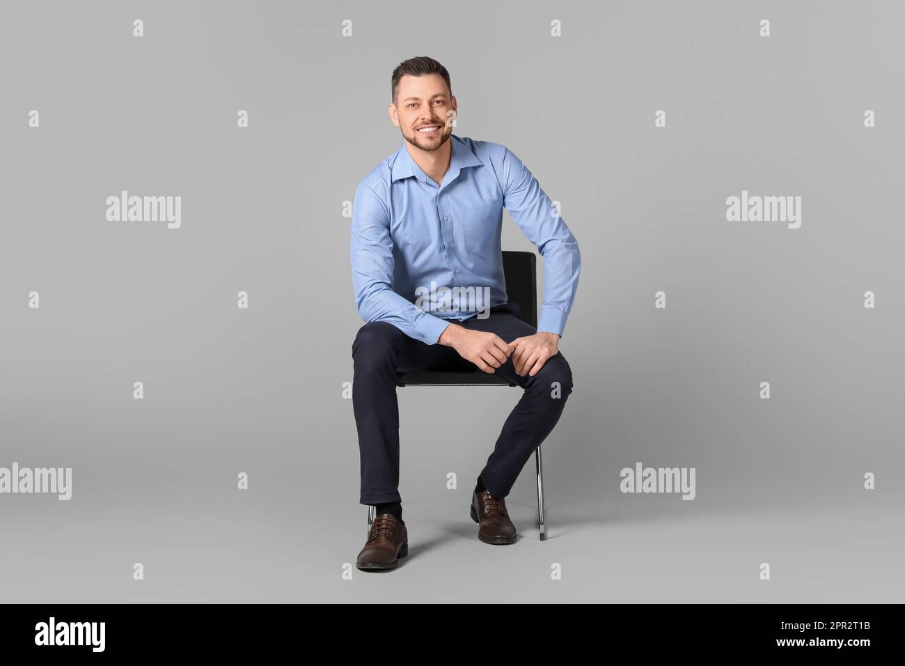 Handsome man sitting in office chair on grey background Stock Photo - Alamy