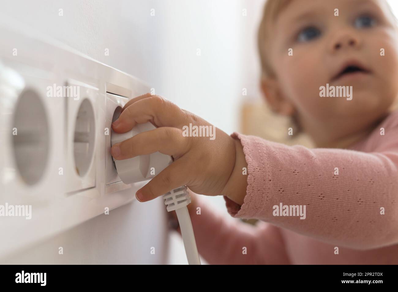 Cute baby playing with electrical socket and plug at home, focus on ...