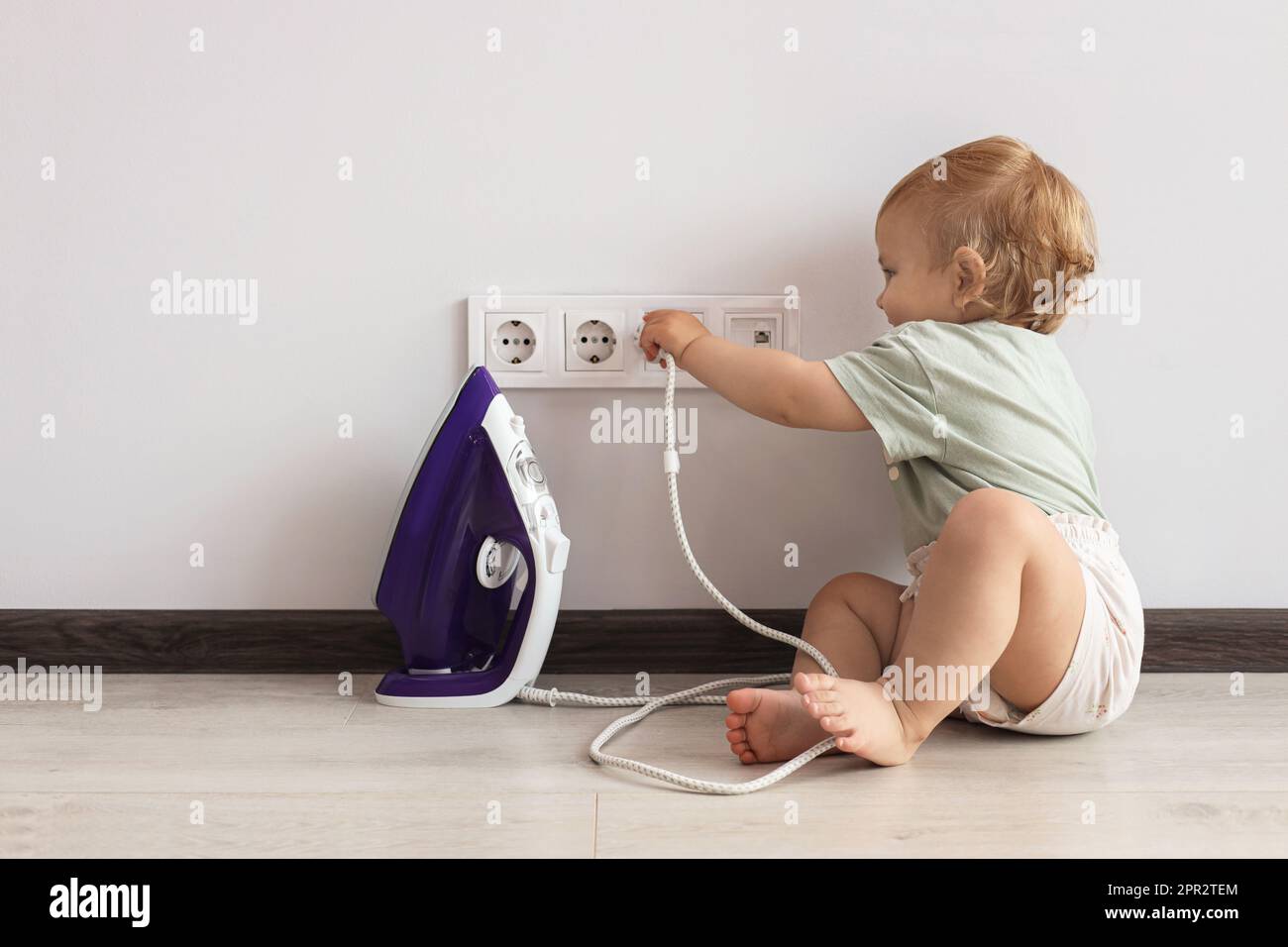 Cute baby playing with electrical socket and iron plug at home ...