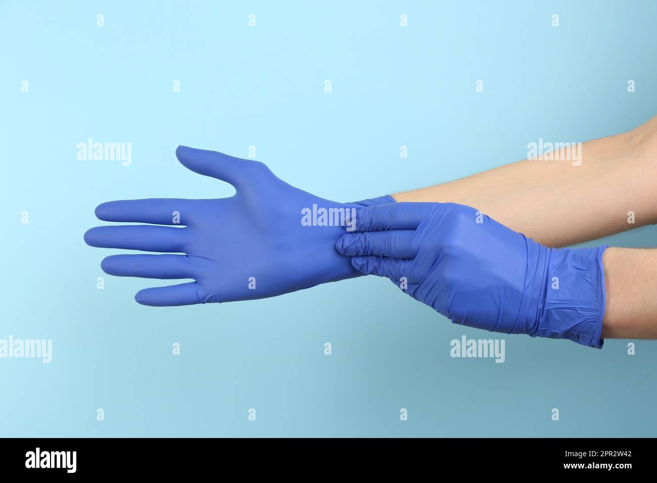 Person putting on medical gloves against light blue background, closeup ...