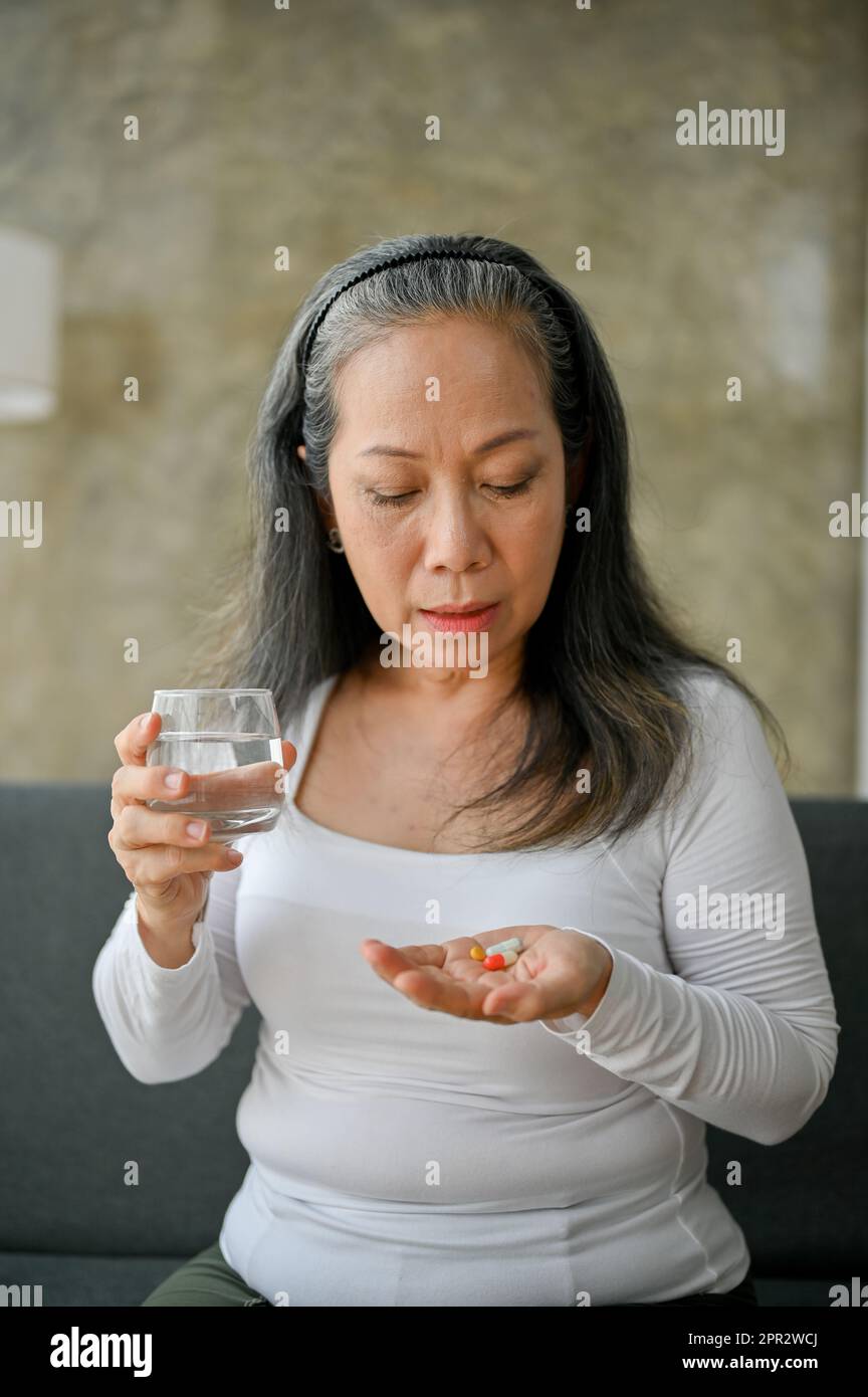 Portrait, Unwell senior woman drinking water and taking her daily ...