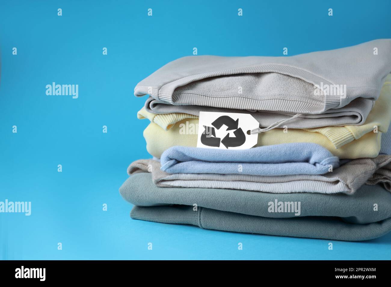 Clothes with recycling label on light blue background, space for text ...