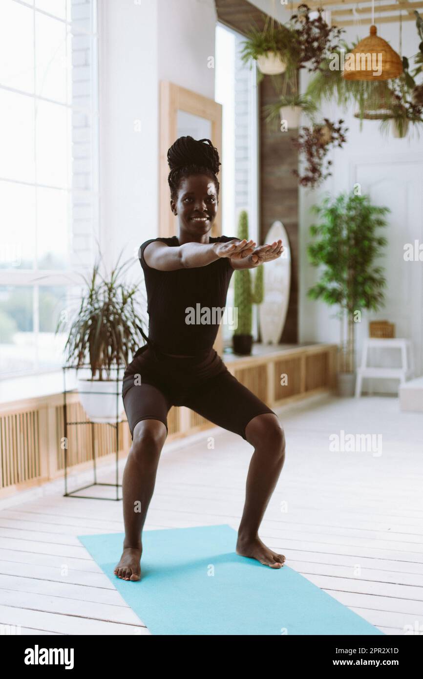 Athletic afro american woman with smile squatting with arms extended ...