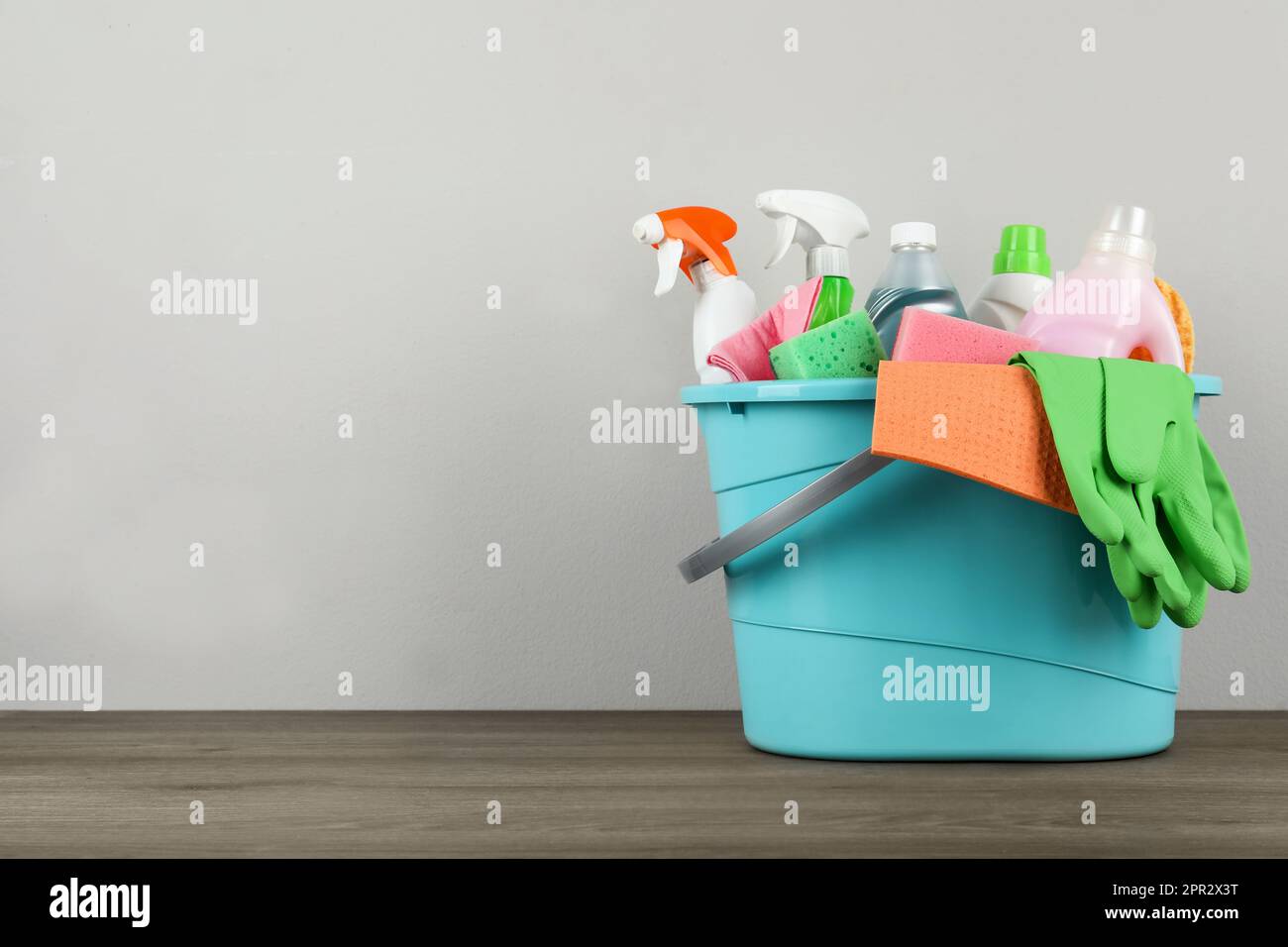 Light blue bucket with cleaning products on wooden table. Space for ...