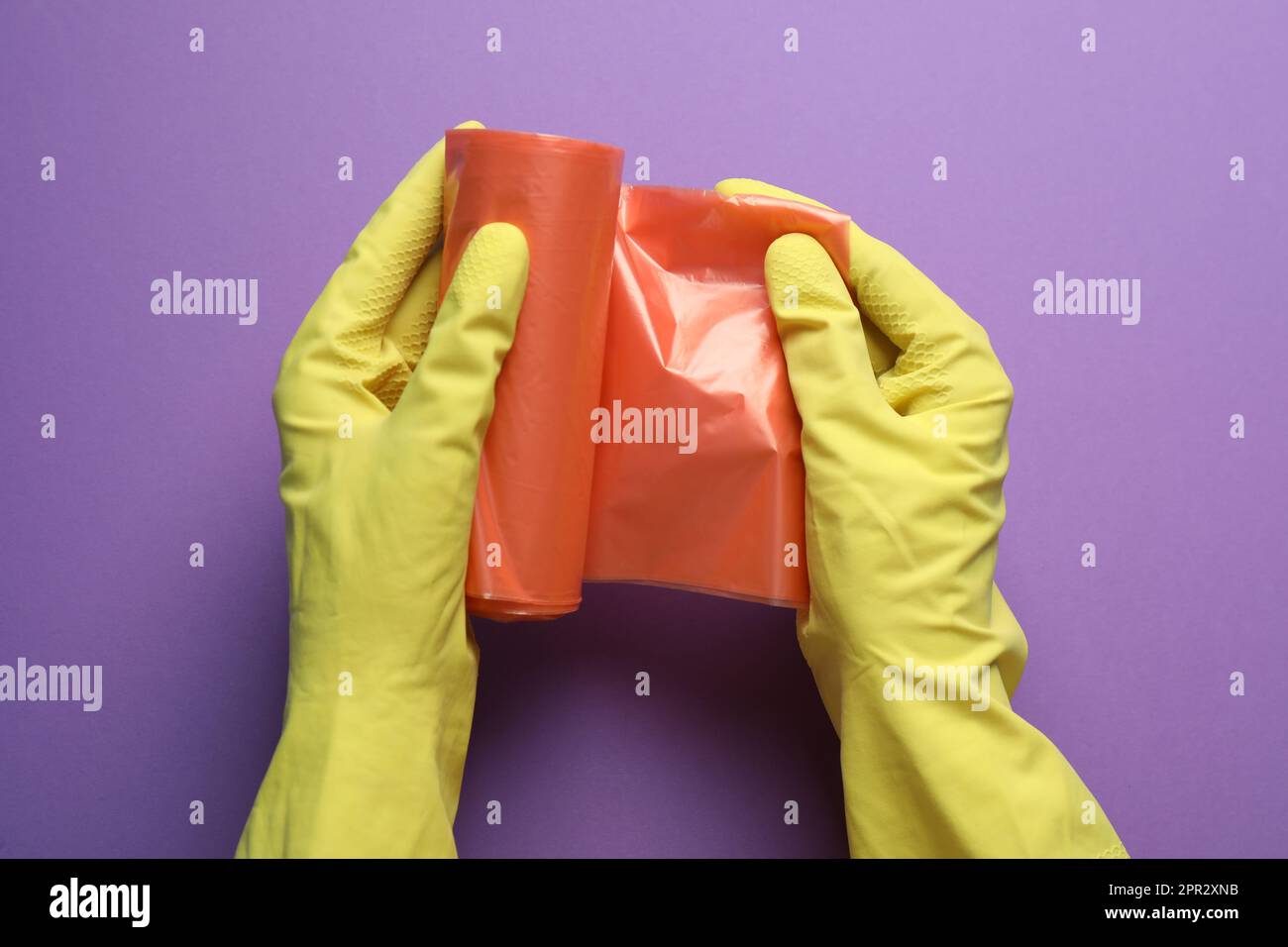 Janitor in rubber gloves holding roll of orange garbage bags over ...