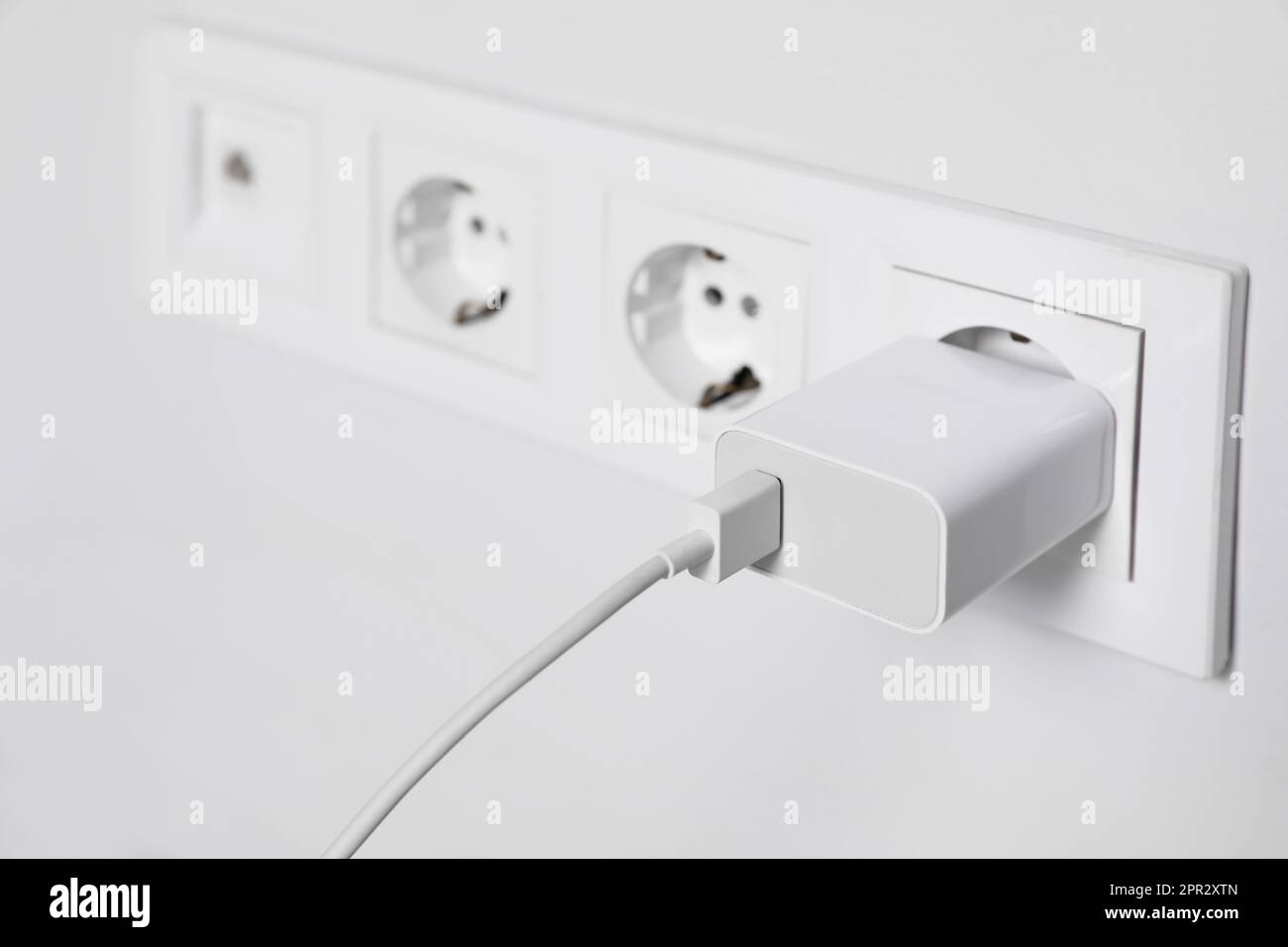 Charger adapter plugged in power socket indoors, closeup. Space for ...