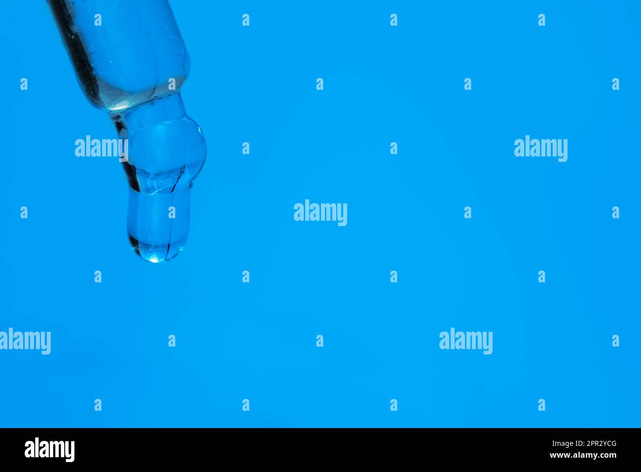 Dripping face serum from pipette on blue background, closeup. Space for ...