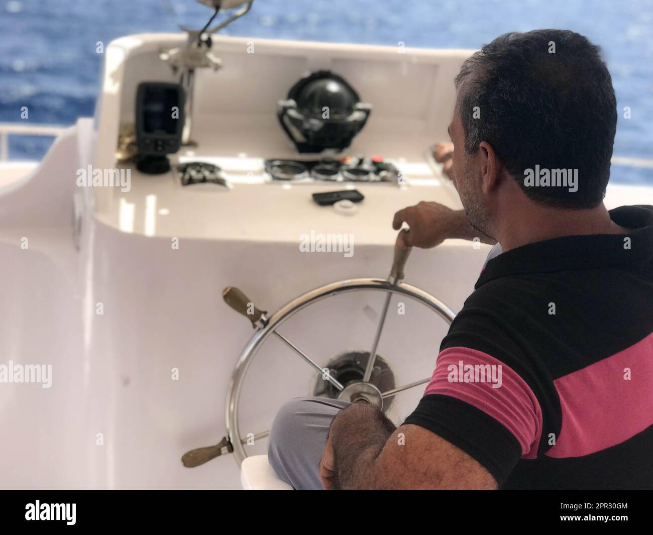 A swarthy captain, an Arab man in a red striped shirt, manages a ship ...