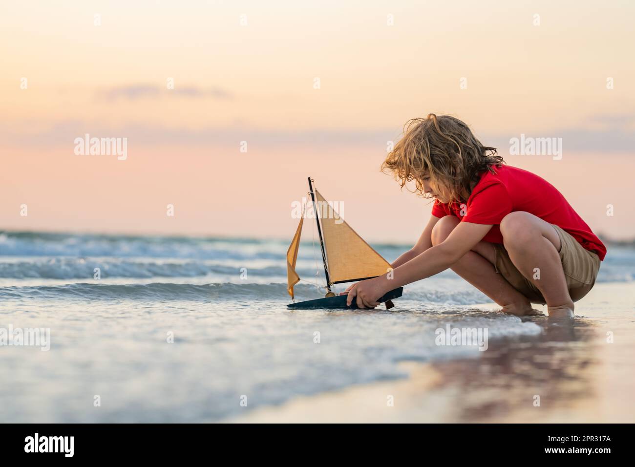 Kid boy playing with toy boat in sea water. Happy holiday by the sea ...