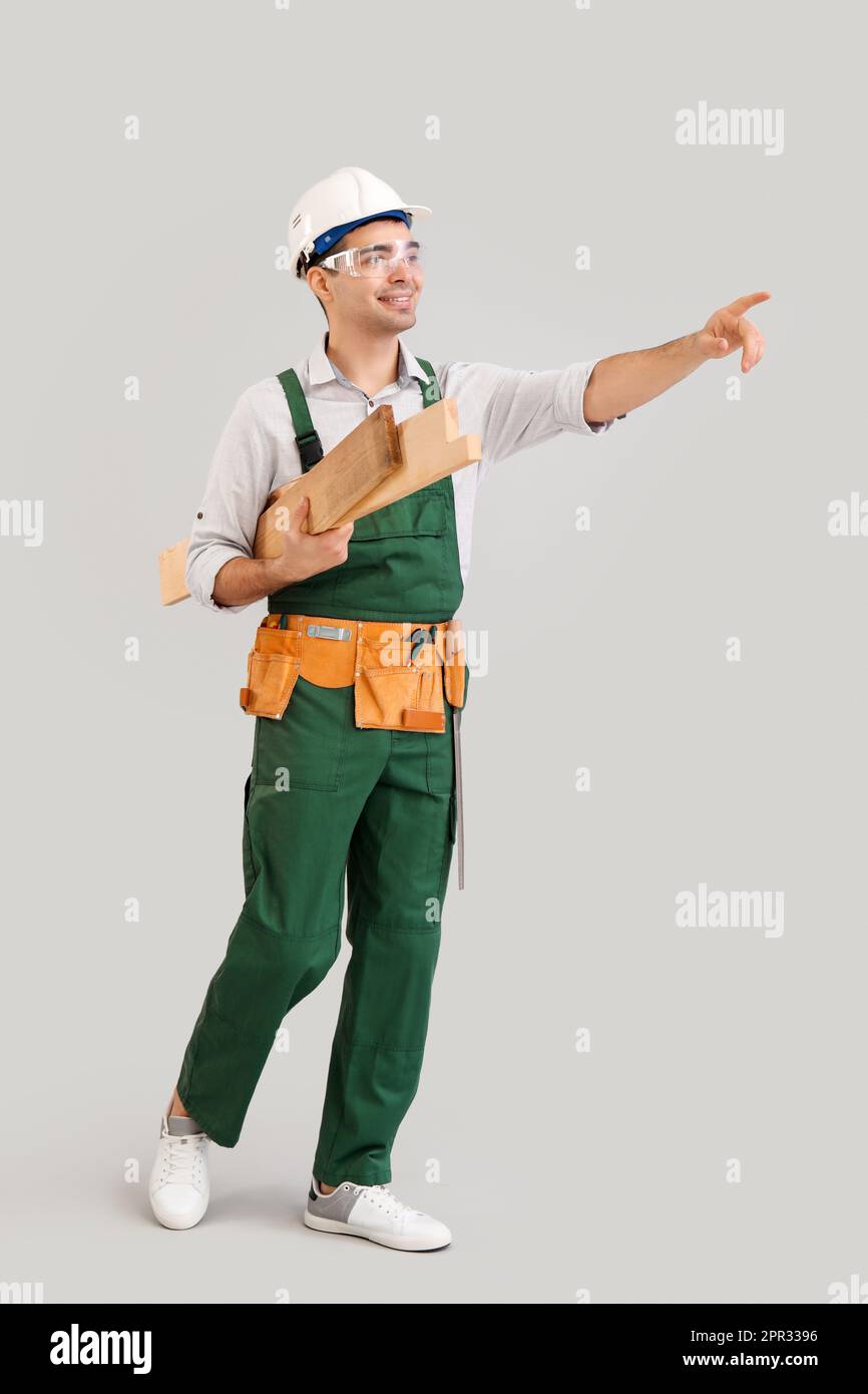 Young carpenter with wooden planks pointing at something on grey ...