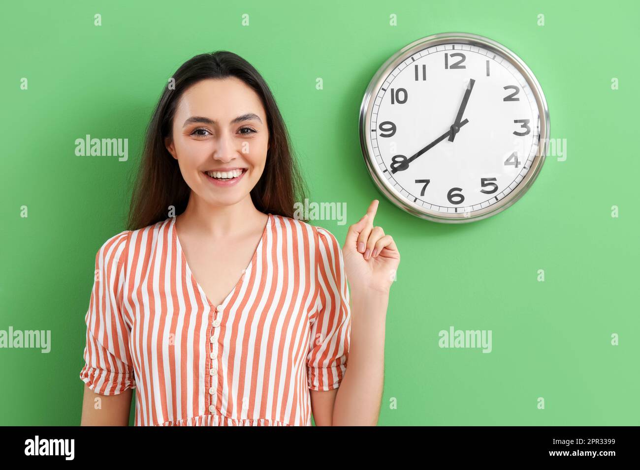 Young woman pointing at clock on green wall Stock Photo - Alamy