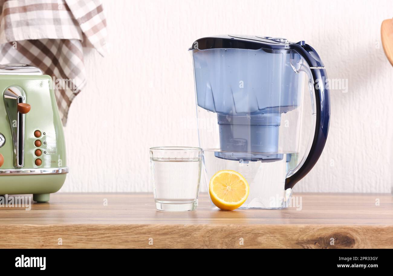 Modern filter jug, glass of water and lemon on kitchen counter Stock ...