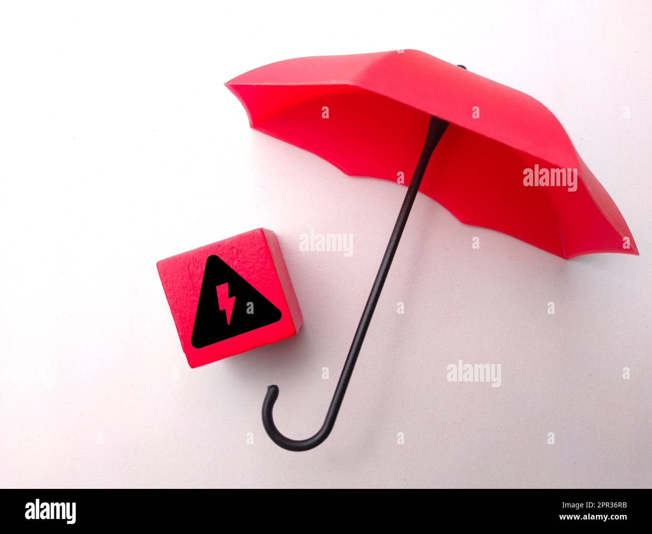 Red umbrella and red cube with an electrical hazard sign on white ...