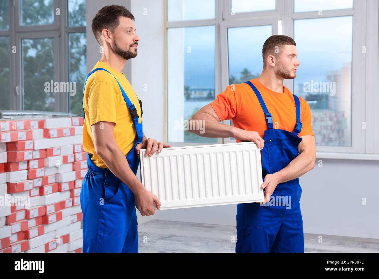 Professional plumbers with new heating radiator indoors Stock Photo - Alamy