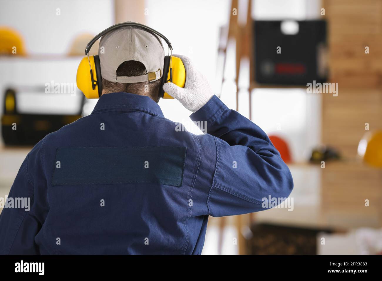 Worker wearing safety headphones indoors, back view. Hearing protection ...