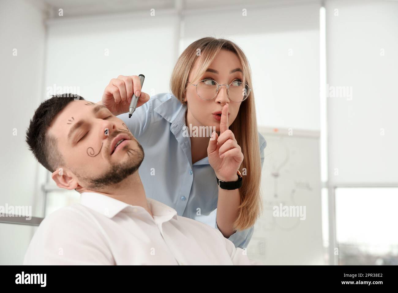 Young woman drawing on colleague's face while he sleeping in office ...