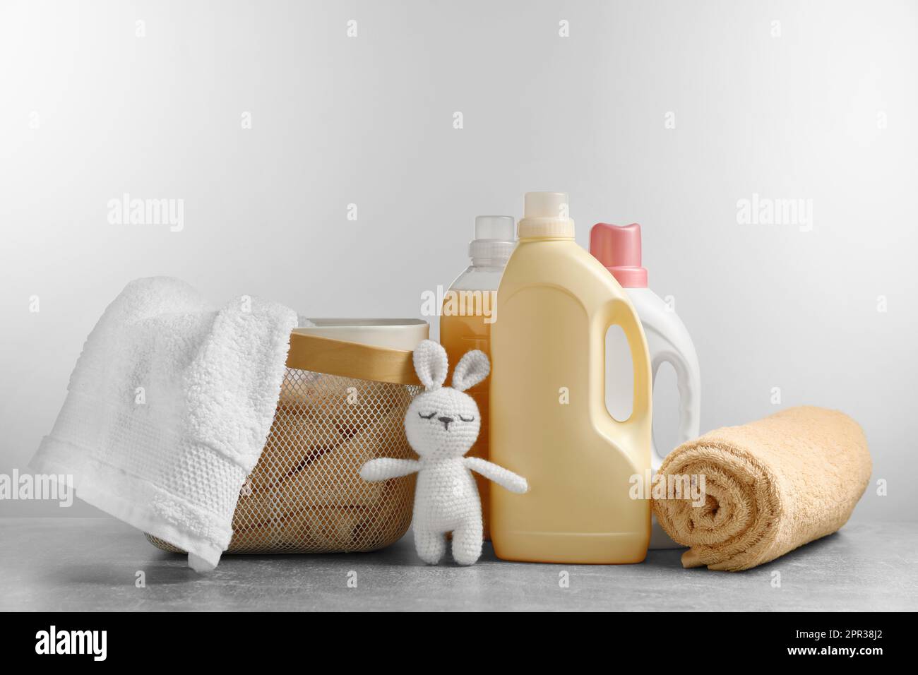Bottles of laundry detergents, fresh towels, knitted rabbit toy on grey ...