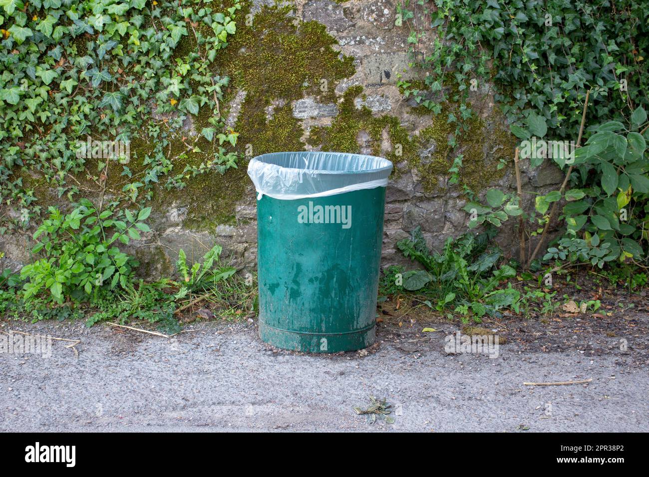 green dust bin with white bin bag at the side of the road next to an ...