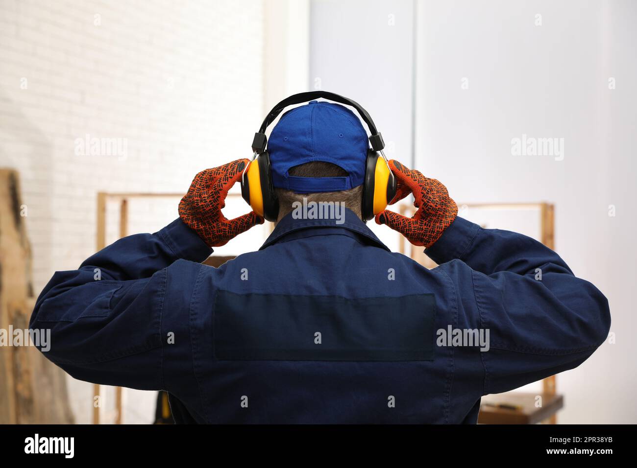 Worker wearing safety headphones indoors, back view. Hearing protection ...