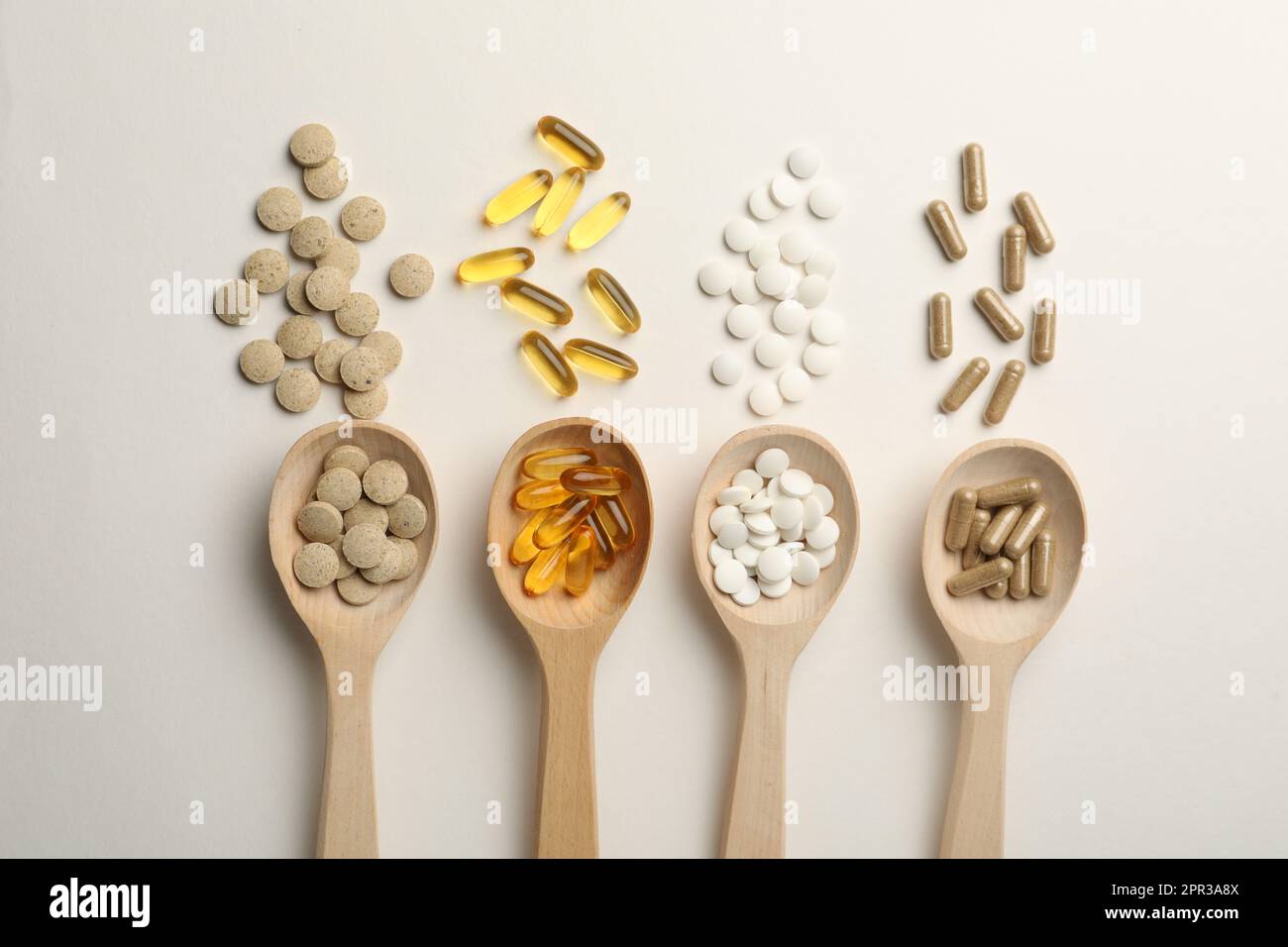 Wooden spoons and different dietary supplements on white background ...