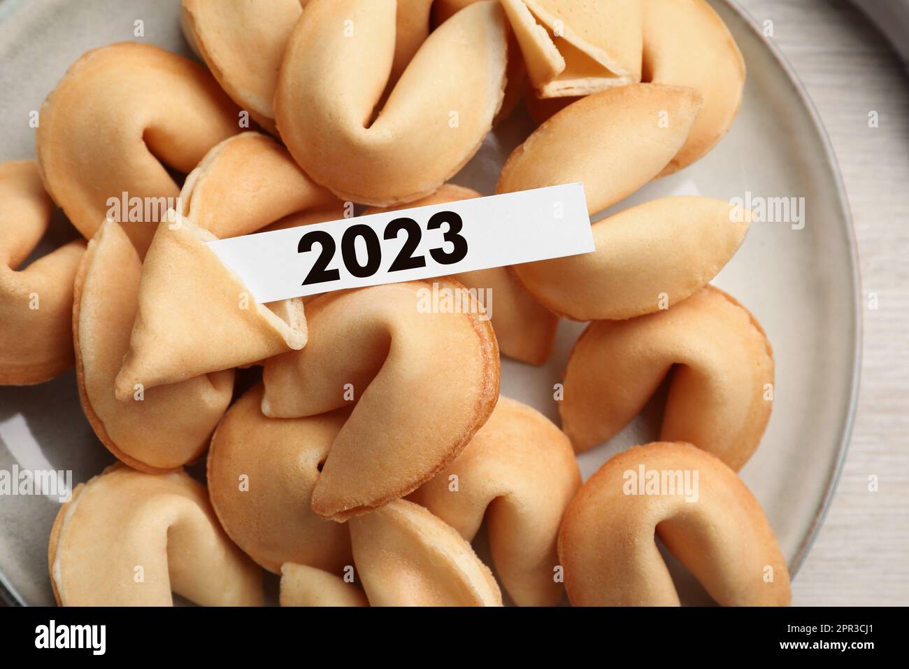 Tasty fortune cookies and paper with number 2023 on plate, top view ...