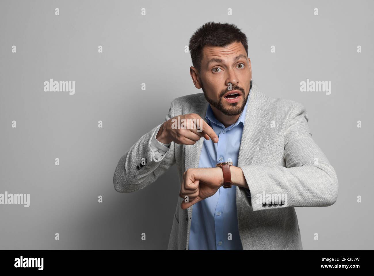 Emotional man checking time on grey background, space for text. Being ...