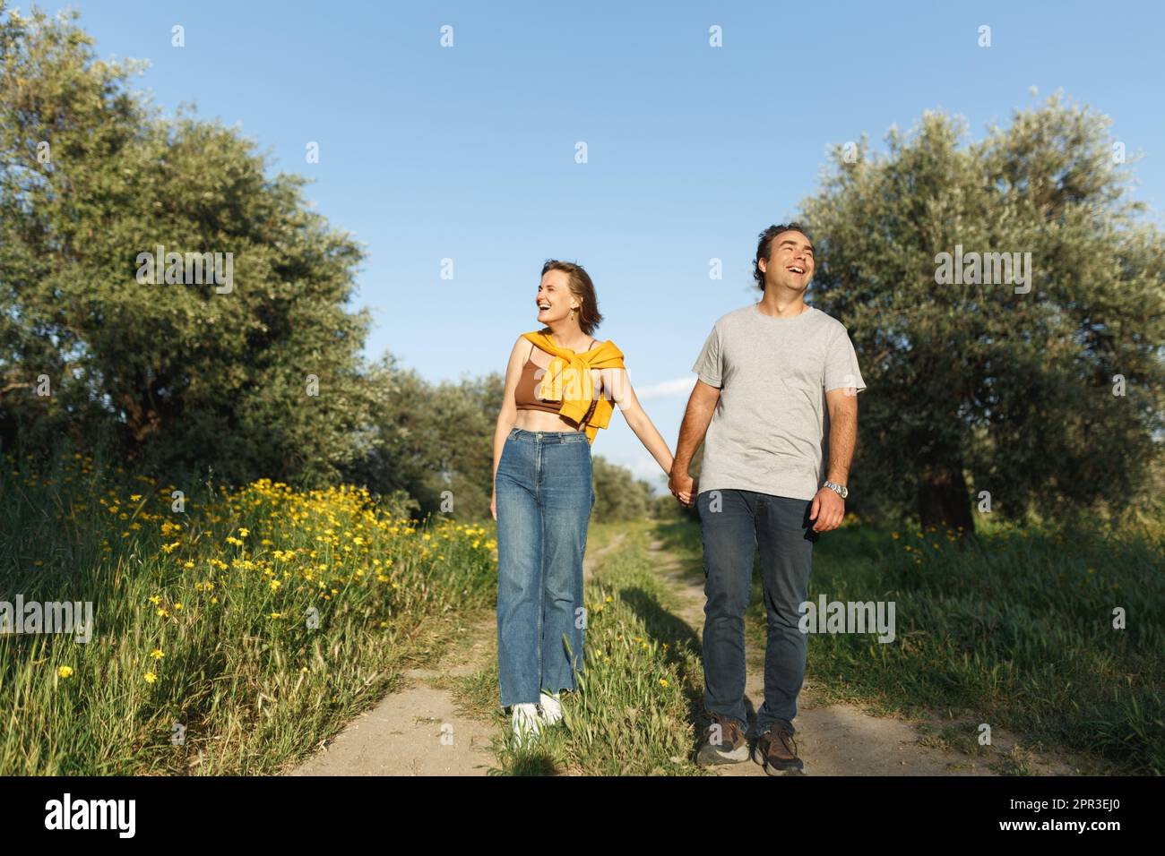 Outdoor shot of young couple in love walking on pathway through grass ...