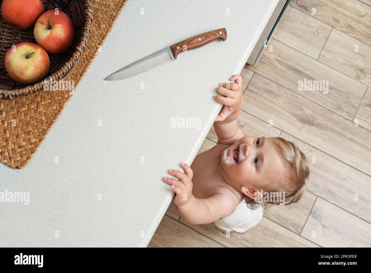Laughing little child reaching for knife on light countertop, above ...