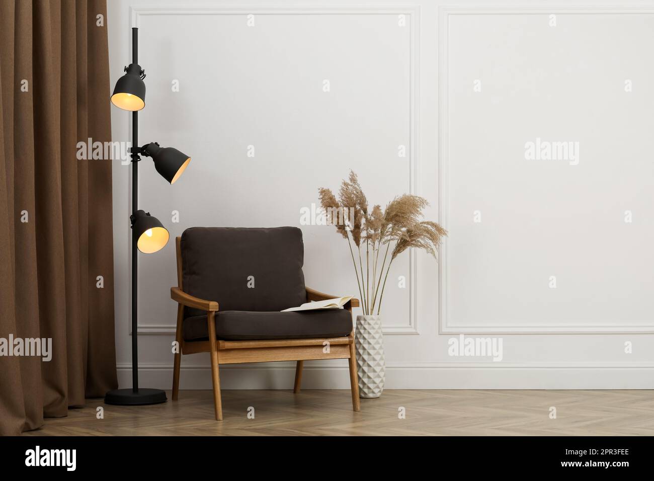 Stylish armchair with book, floor lamp and spikes near white wall ...