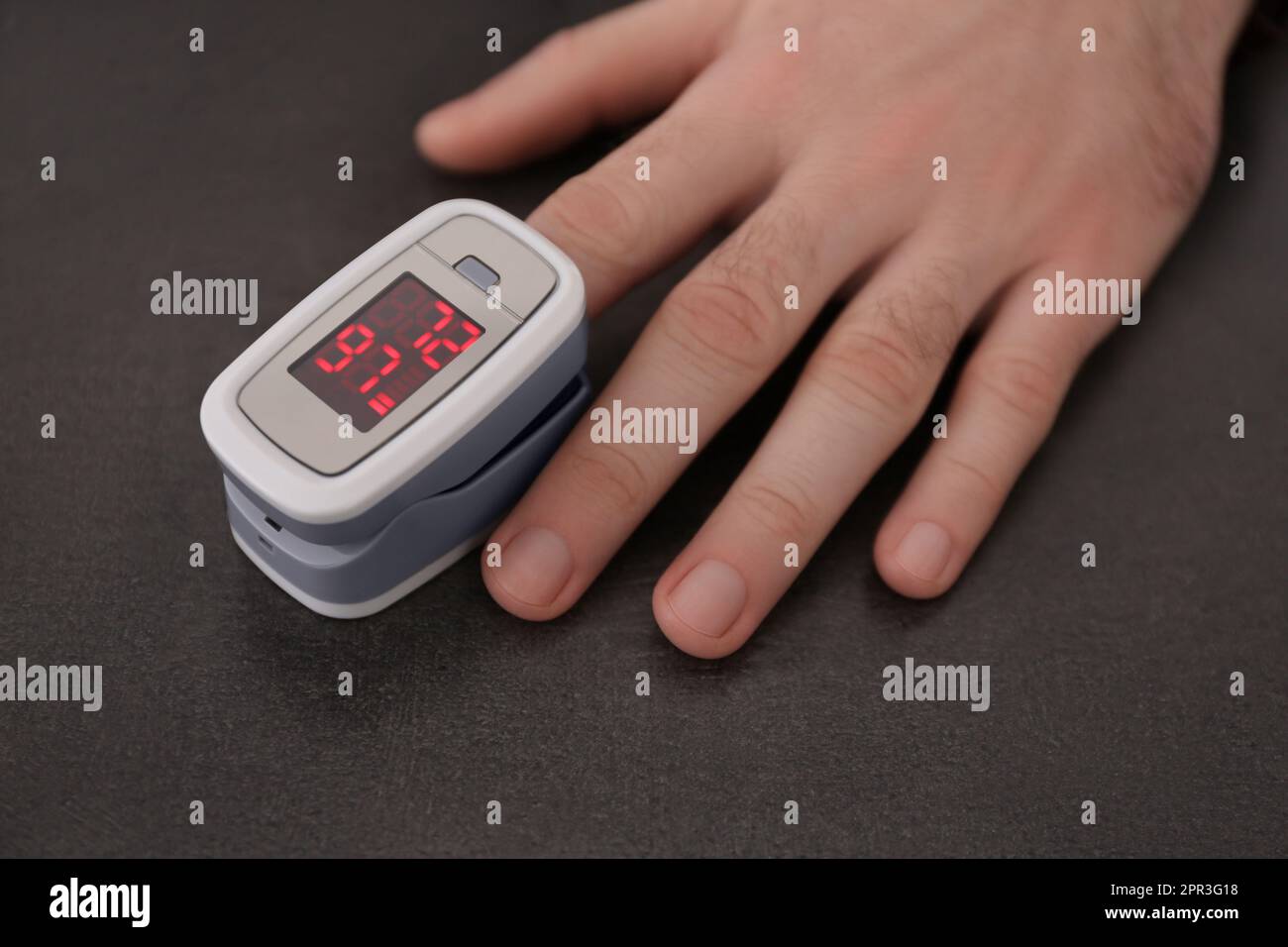 Man measuring oxygen level with modern fingertip pulse oximeter at grey ...