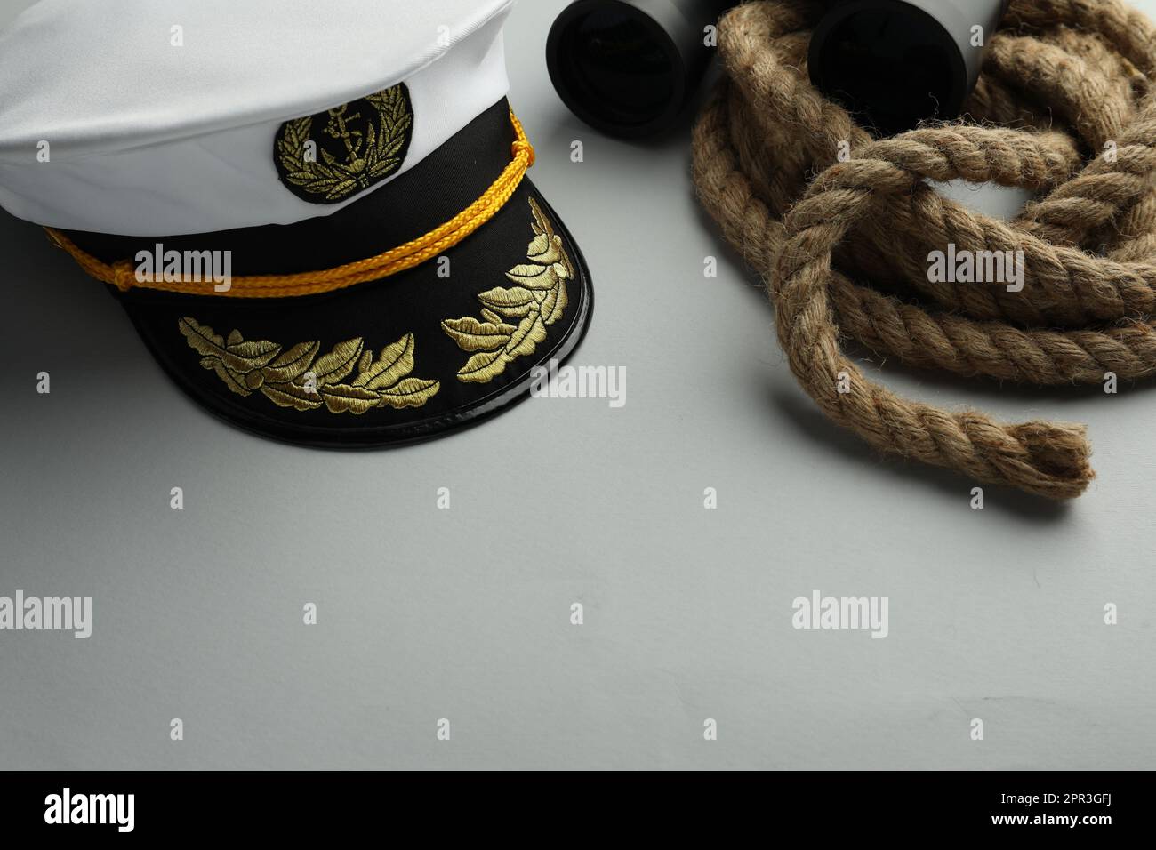 Peaked cap, rope and binoculars on light grey background. Space for ...