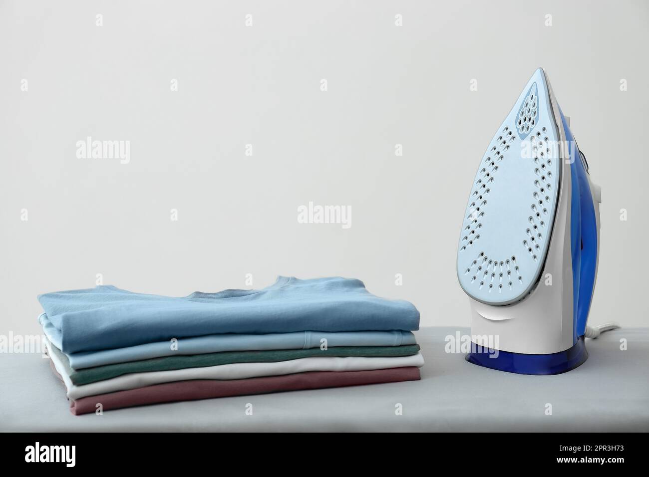 Modern iron and stack of clean clothes on board against white ...