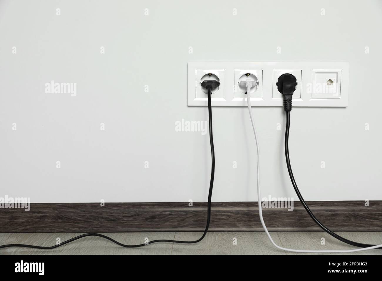 Power sockets with inserted plugs on white wall indoors, space for text ...